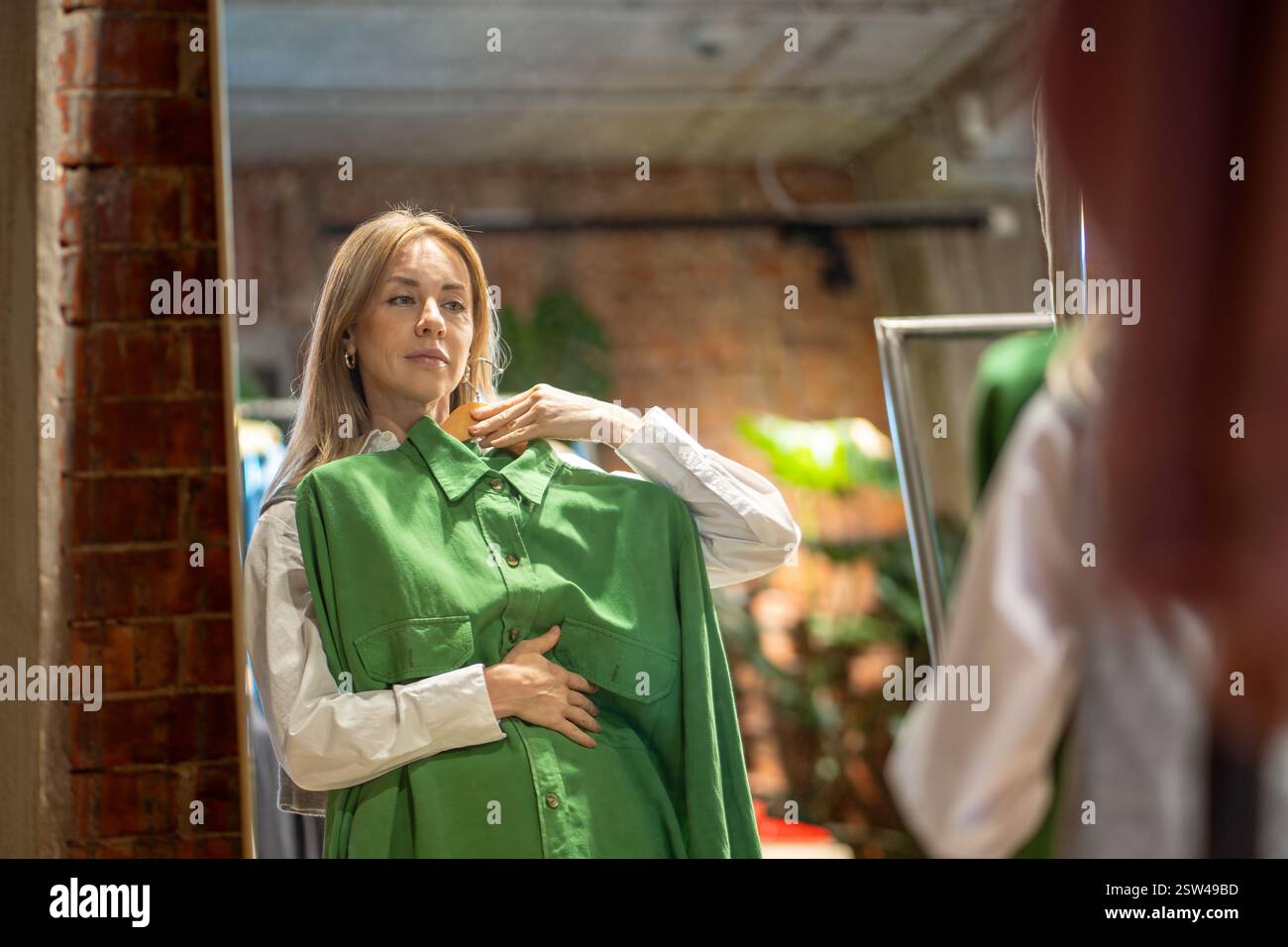Content woman choose clothes, try shirt in mirror at shopping center ...