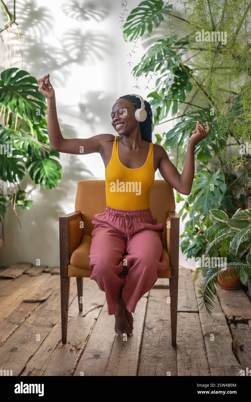 Joyful black woman dancing sitting on chair hearing favourite music ...