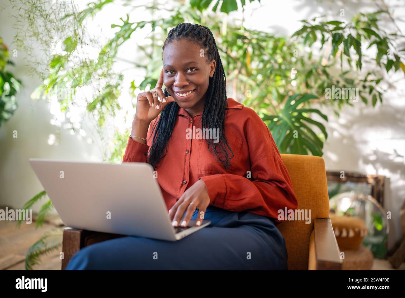 Happy pleased black woman with laptop on laps sitting on chair in sunny ...