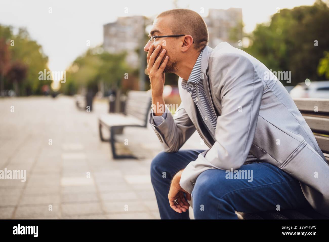 Portrait of thoughtful and worried man. He is sitting on bench in the ...