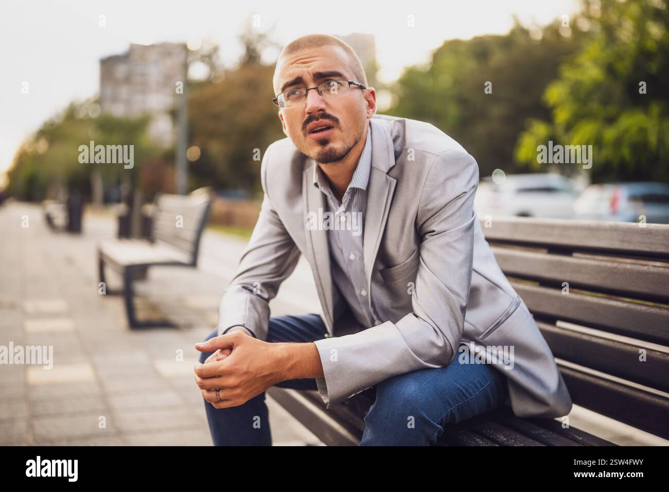 Portrait of thoughtful and worried man. He is sitting on bench in the ...