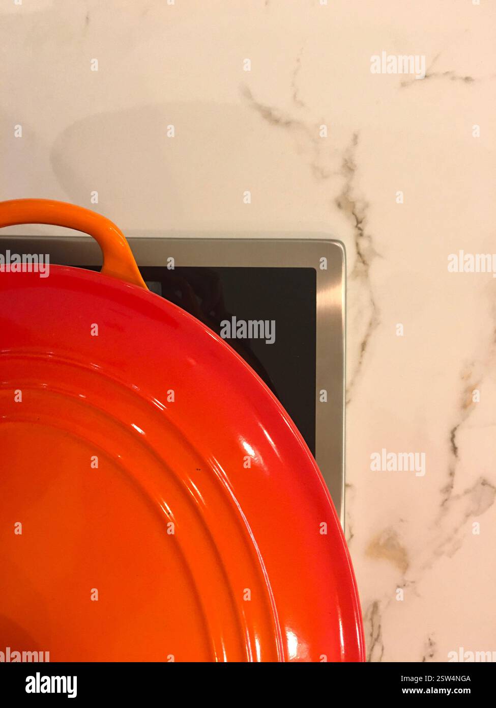A vibrant orange cast iron pot on an induction cooktop, set against a ...