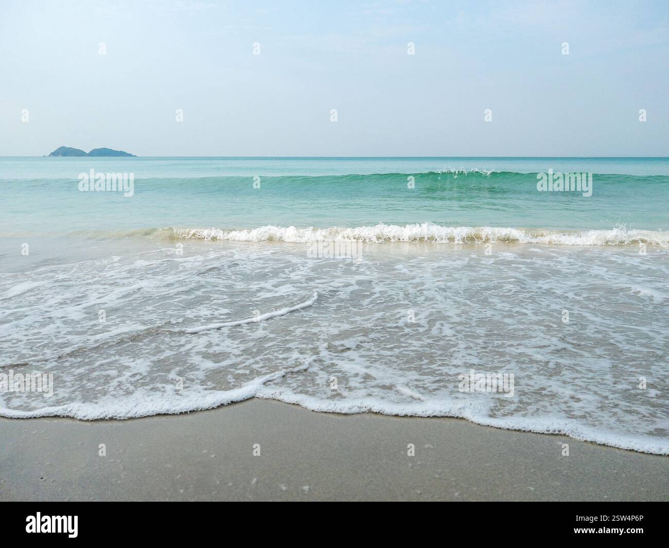 Soft white foam rolls onto the smooth sandy shore as gentle waves meet ...
