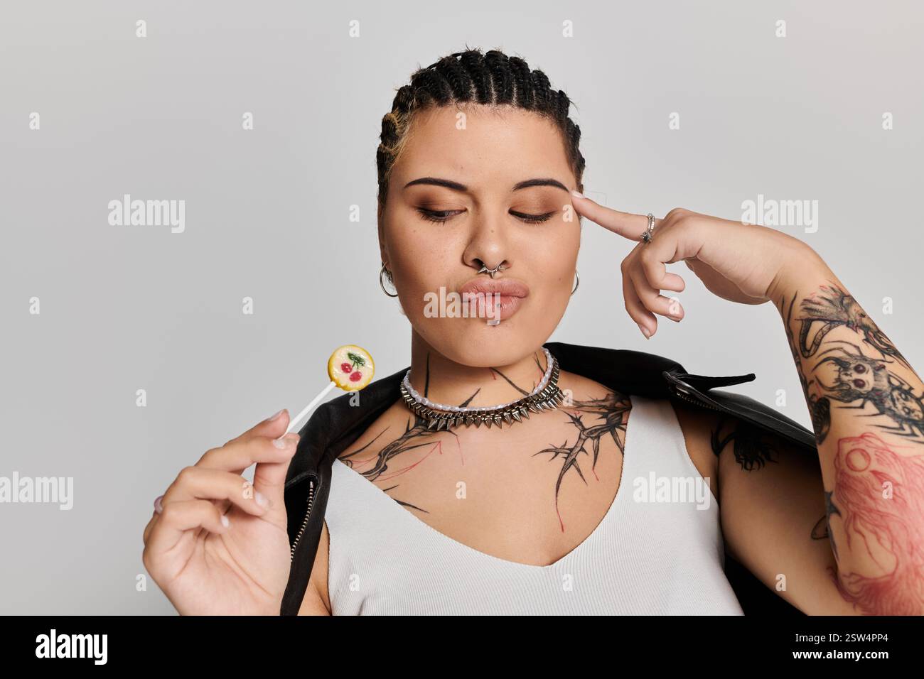 A confident young woman with bold tattoos poses with a lollipop ...
