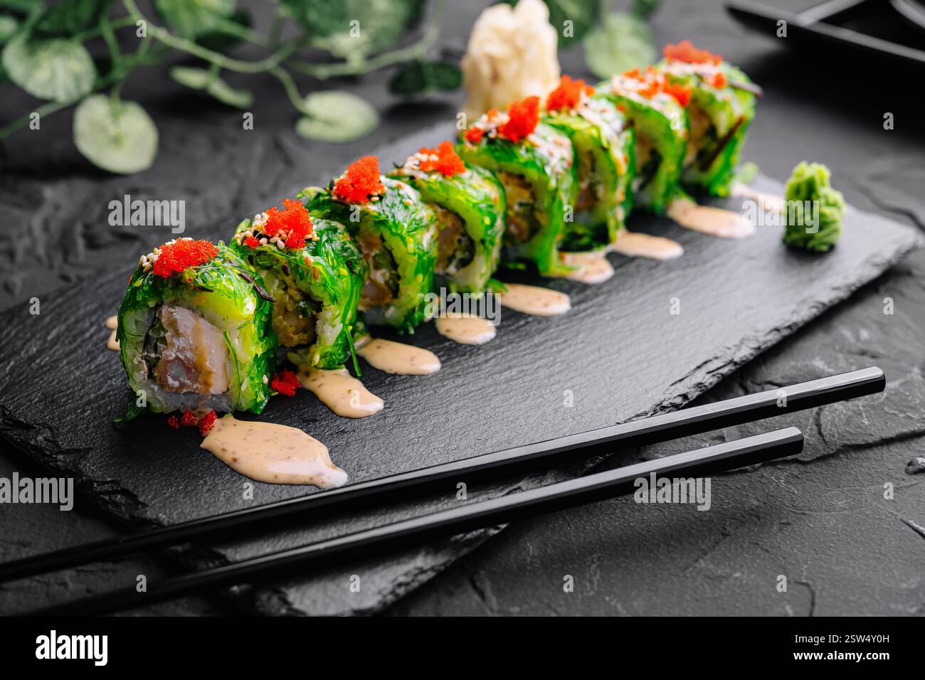 Delectable sushi roll topped with tobiko and spicy mayo on a dark slate ...