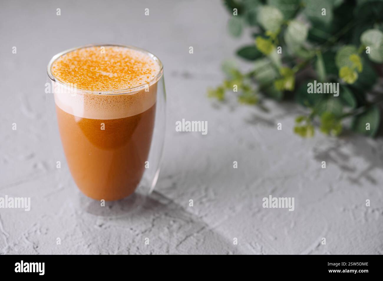 Glass cup of frothy spiced tea latte on a gray textured surface with ...