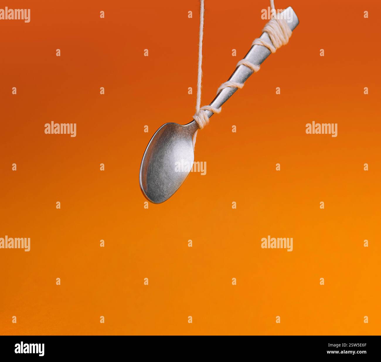 Silver spoon tied with string against a vibrant orange backdrop ...