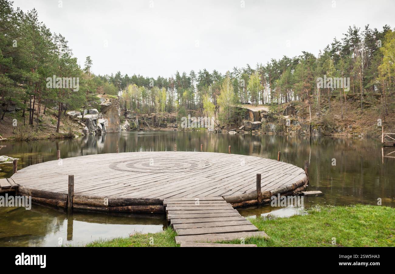 Circular pier at the edge of quarry lake in pine forest. Round ...