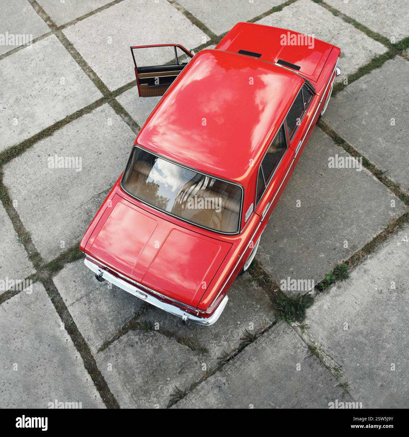 Red 1970s sedan on concrete-paved surface. Aerial rear three quarter ...