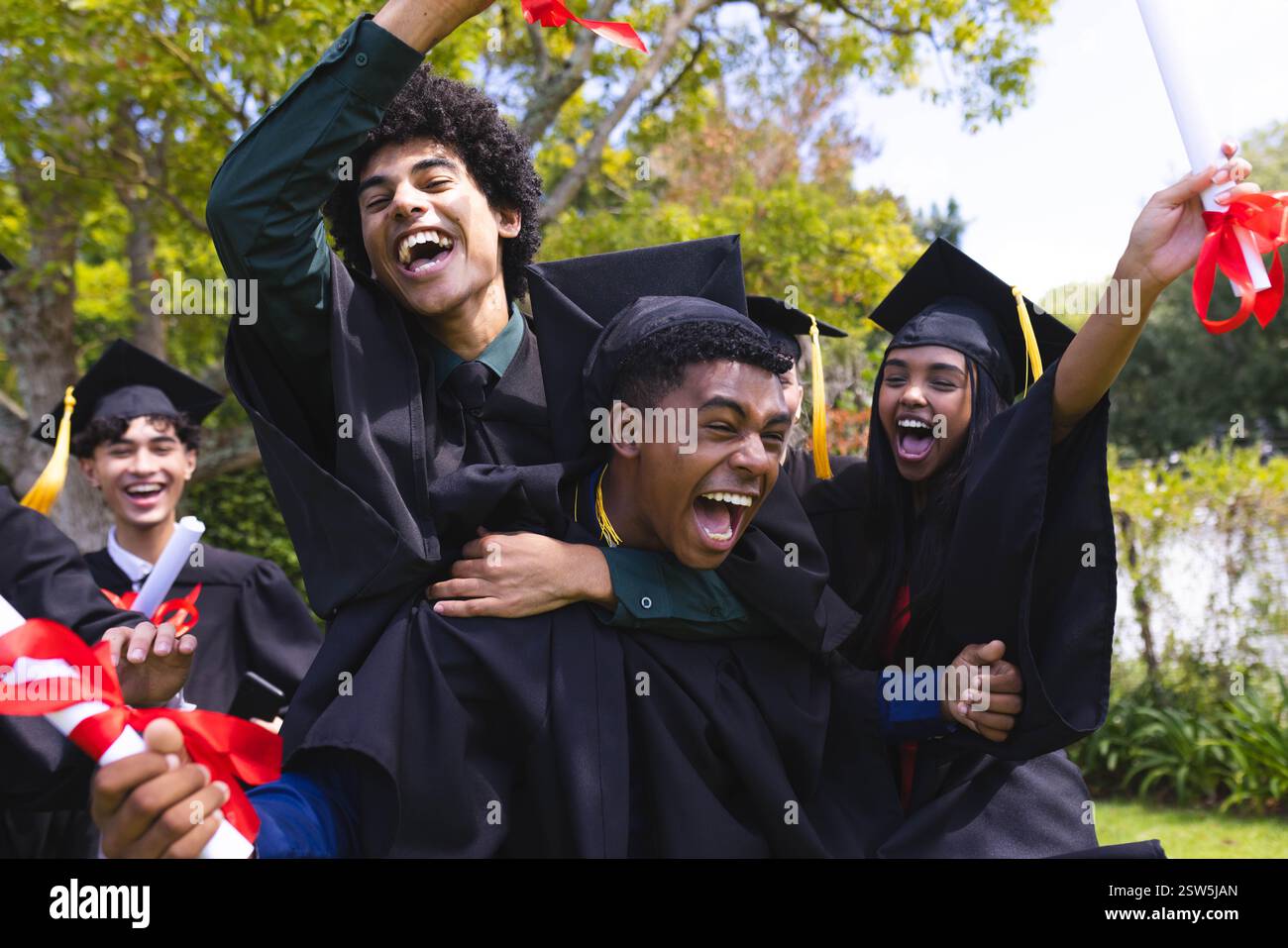 Graduating diverse students wearing caps and gowns celebrating in ...