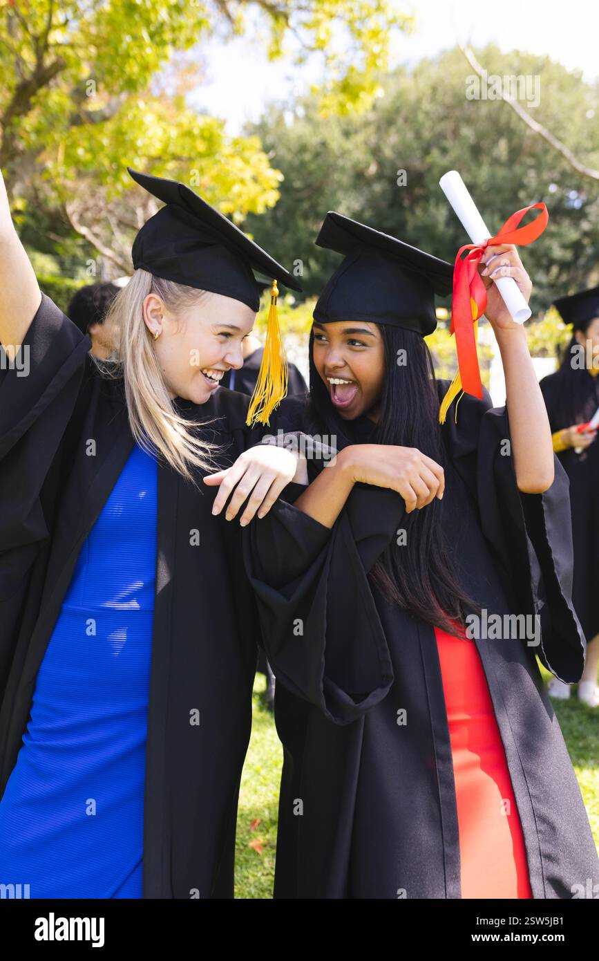 Graduating diverse students celebrating in garden, wearing caps and gowns, feeling excited ...