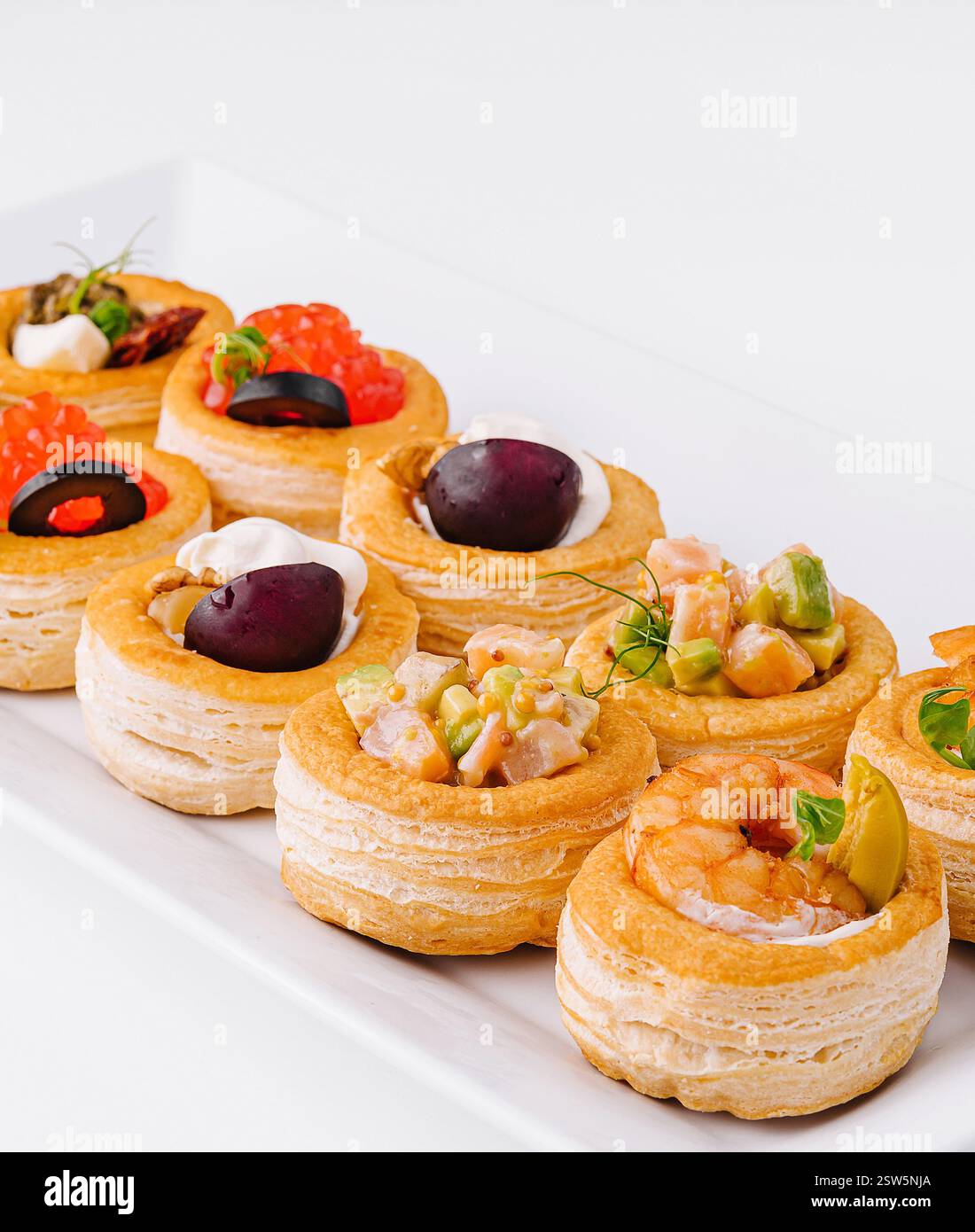 Selection of elegant mini tartlets with savory toppings on a sleek ...