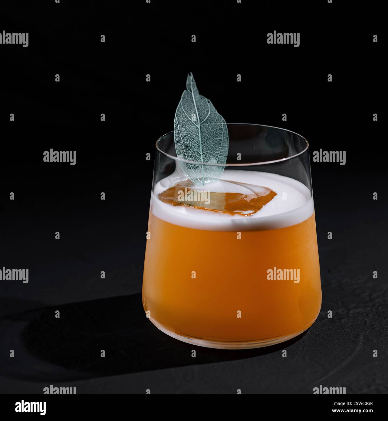 Modern cocktail featuring a frothy top and a delicate leaf garnish ...