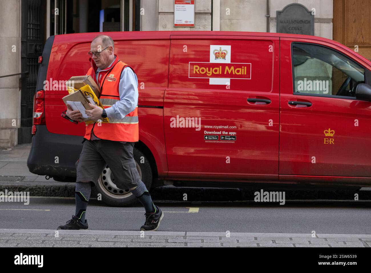Royal Mail postman carrying packages from his van across Pall Mall in ...