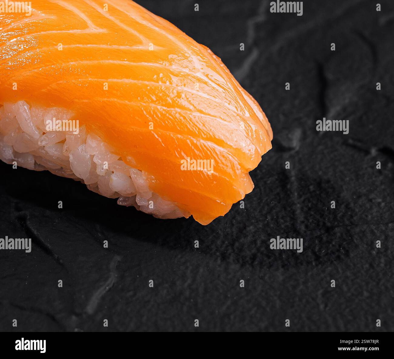 Close-up of a single salmon nigiri sushi piece on a textured slate ...