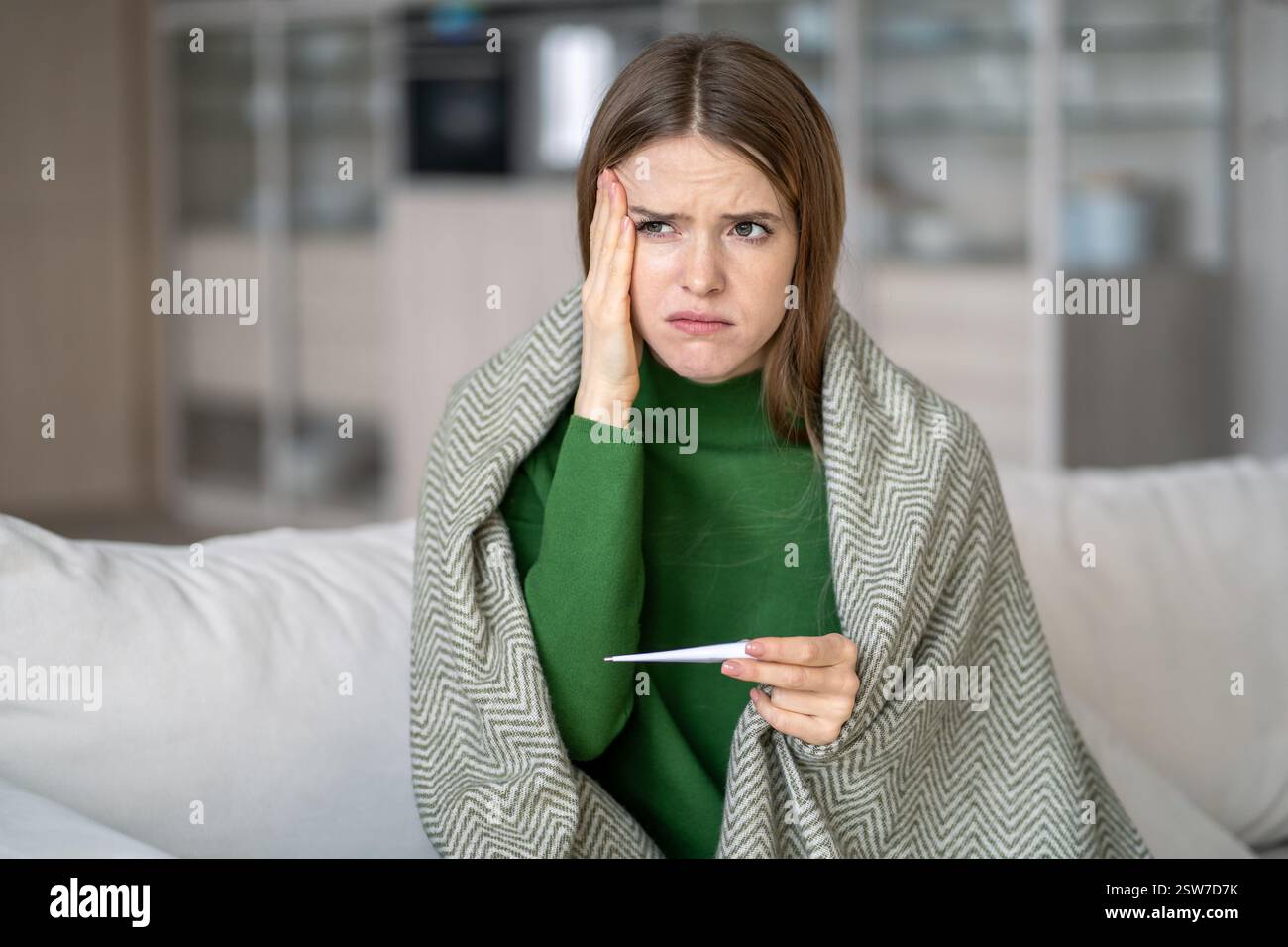 Frustrated woman measures fever on sofa, feeling weak and dizzy at home ...