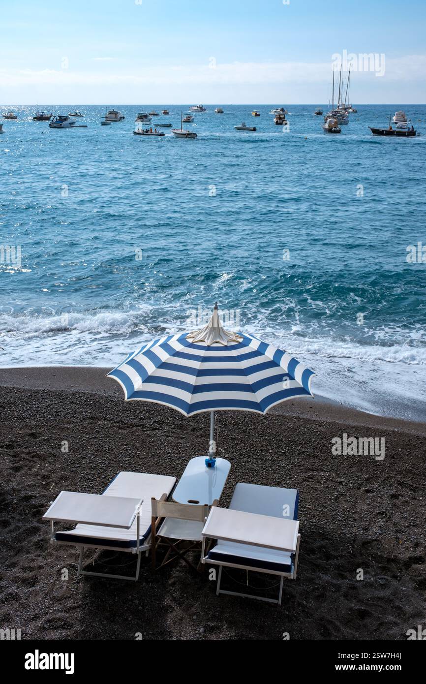 A tranquil beach setup awaits, featuring a blue-striped umbrella and ...