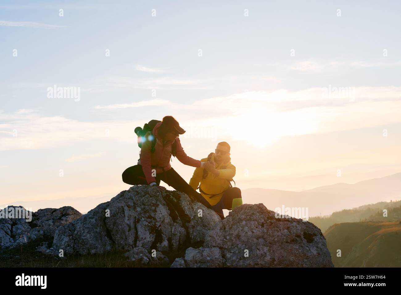Two hikers, couple in outdoor gear climb rocky terrain with the sun ...