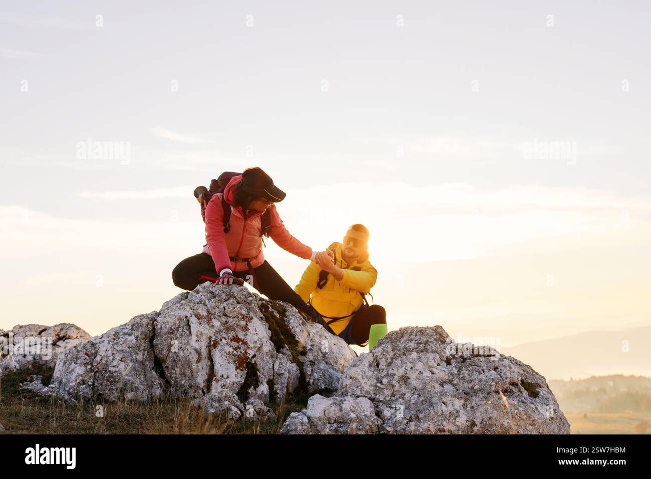Two hikers, couple in outdoor gear climb rocky terrain with the sun ...