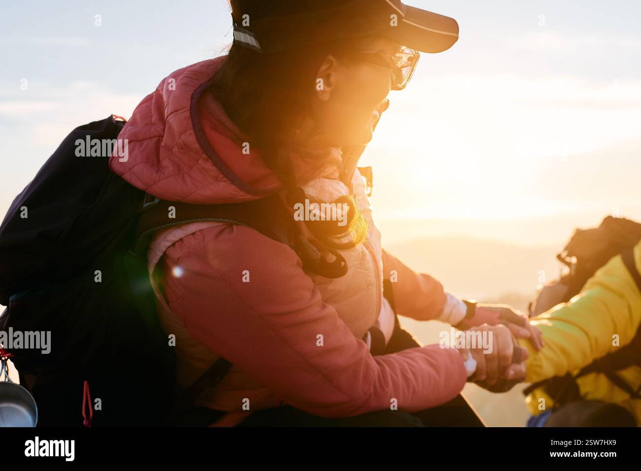 A hiker helps a friend climb the mountain at sunrise.A man in a yellow ...