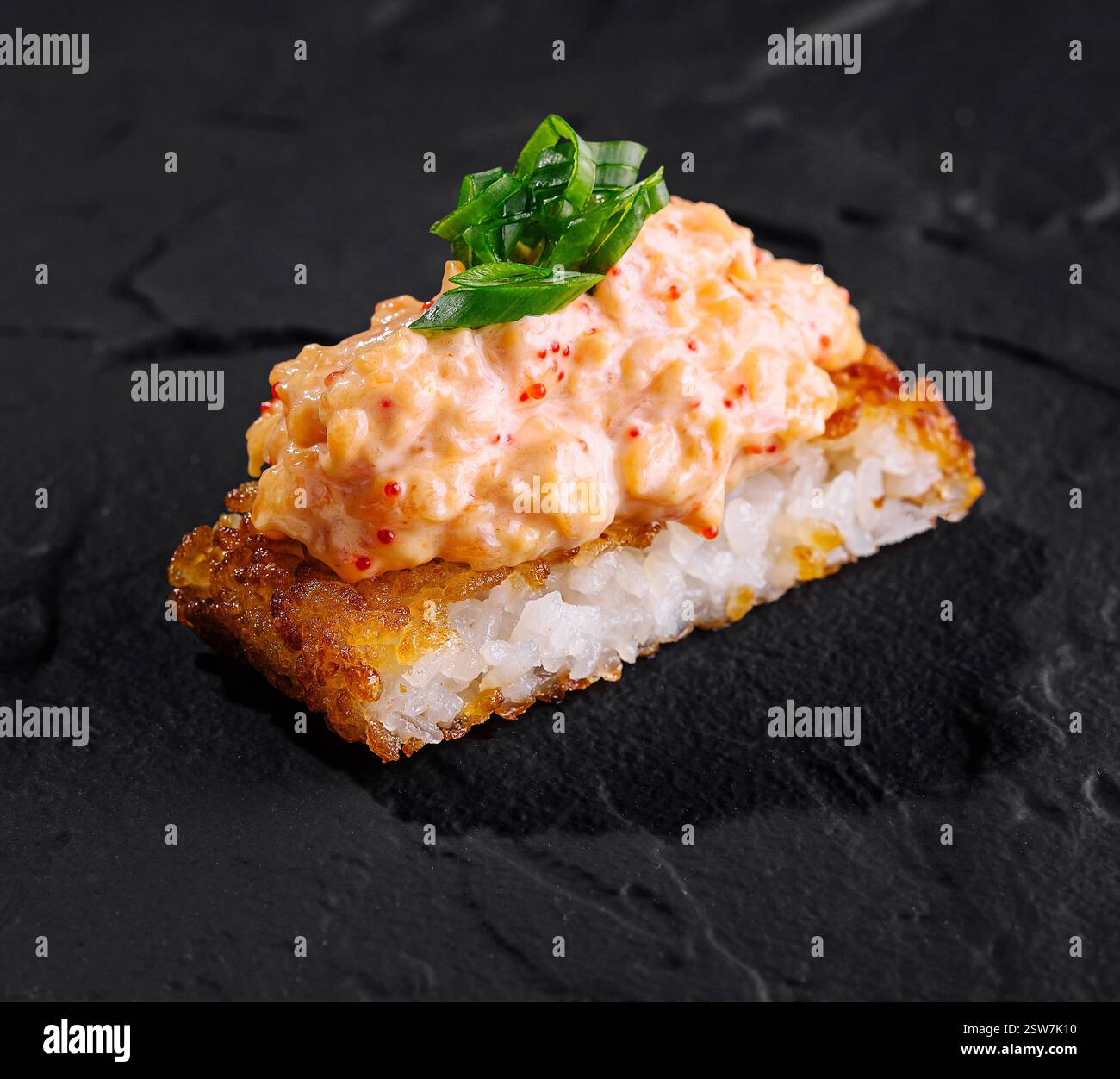 Single piece of spicy sushi roll topped with green garnish on a dark ...