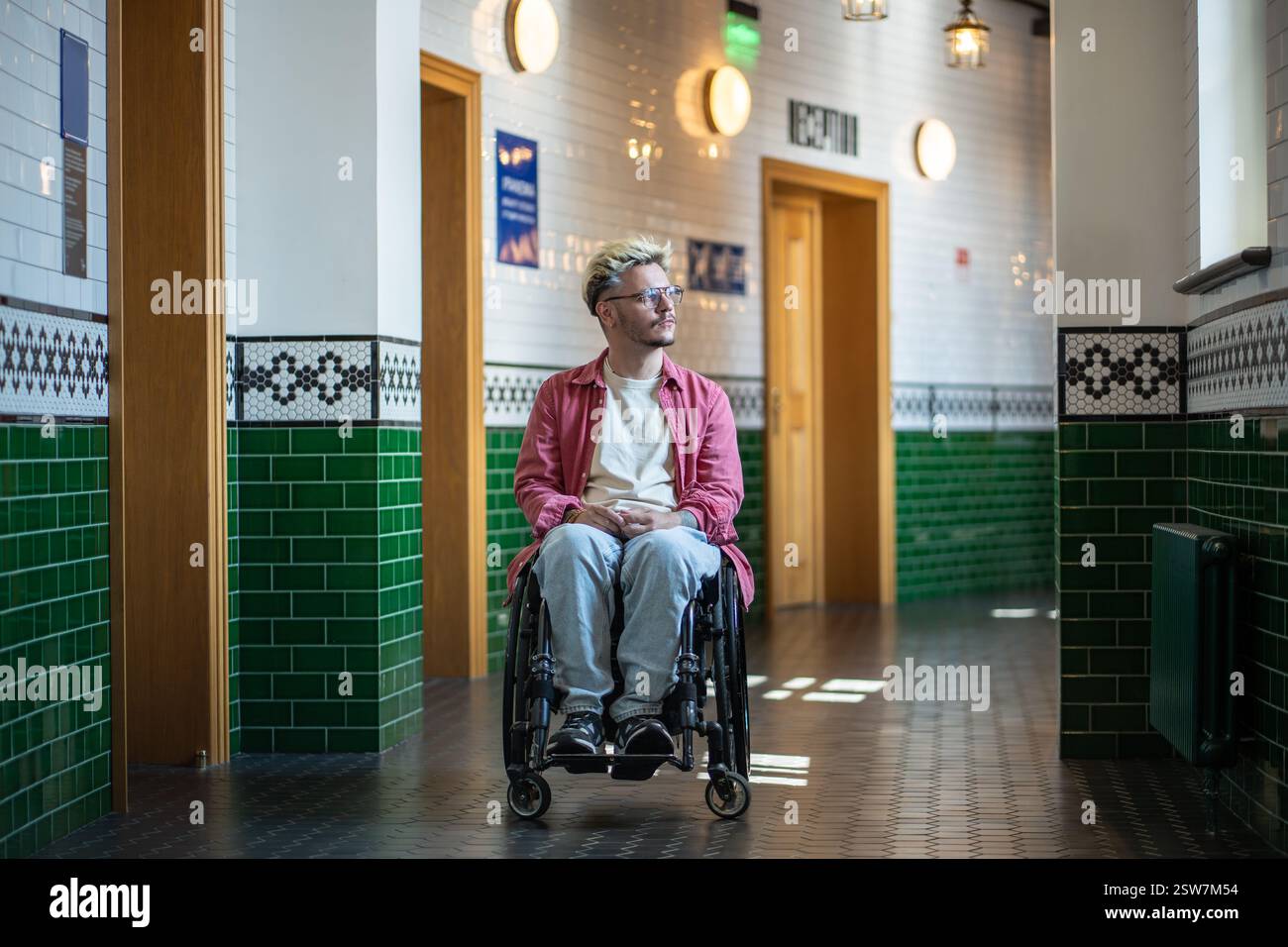 Thoughtful man student in wheelchair pauses in hallway near university ...