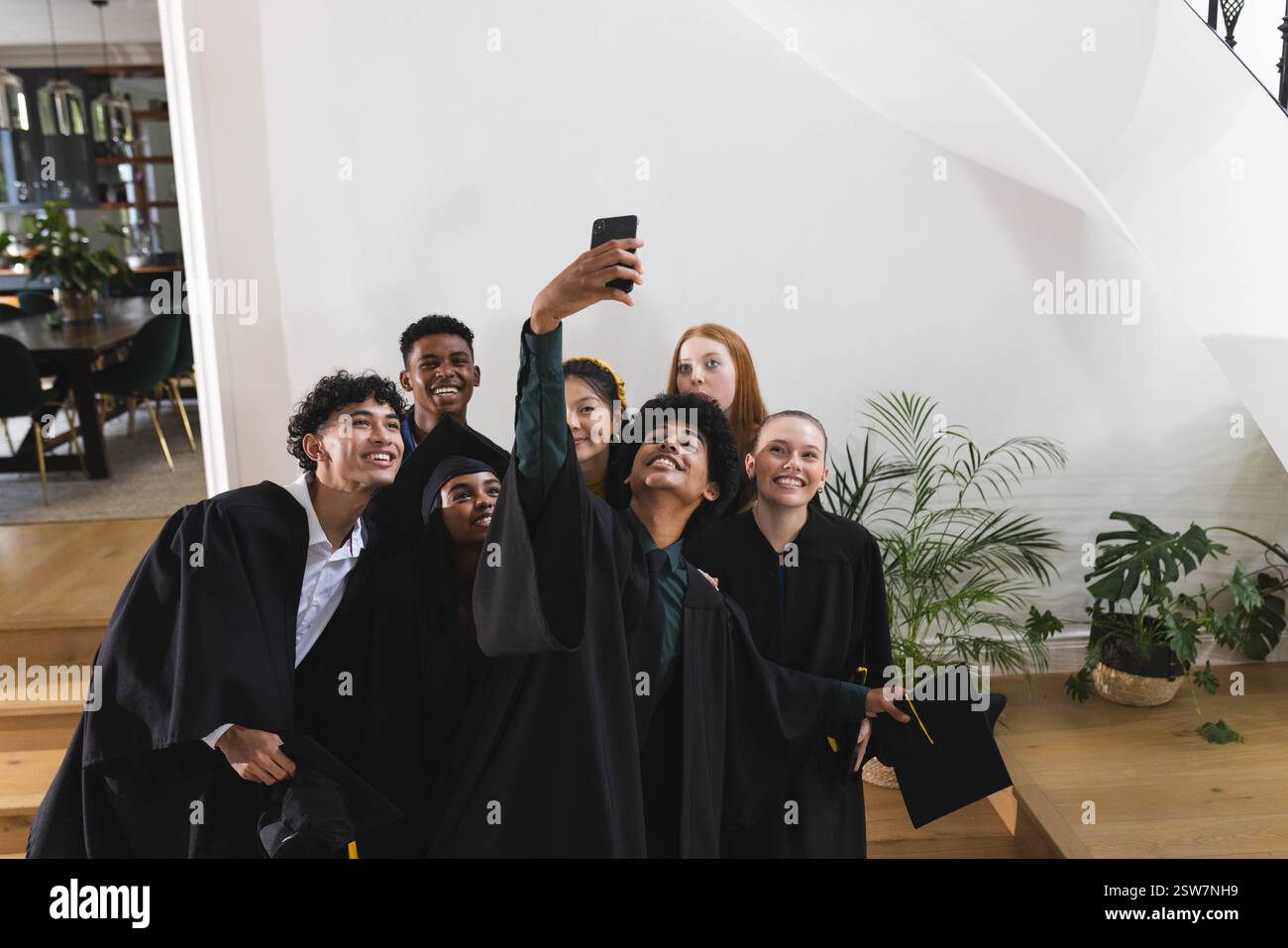 Graduating diverse students taking selfie in caps and gowns ...