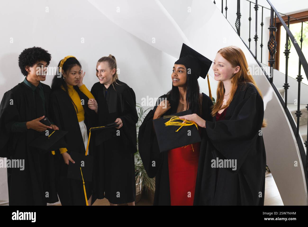 Graduating diverse students in caps and gowns celebrating together with joy and laughter, at ...
