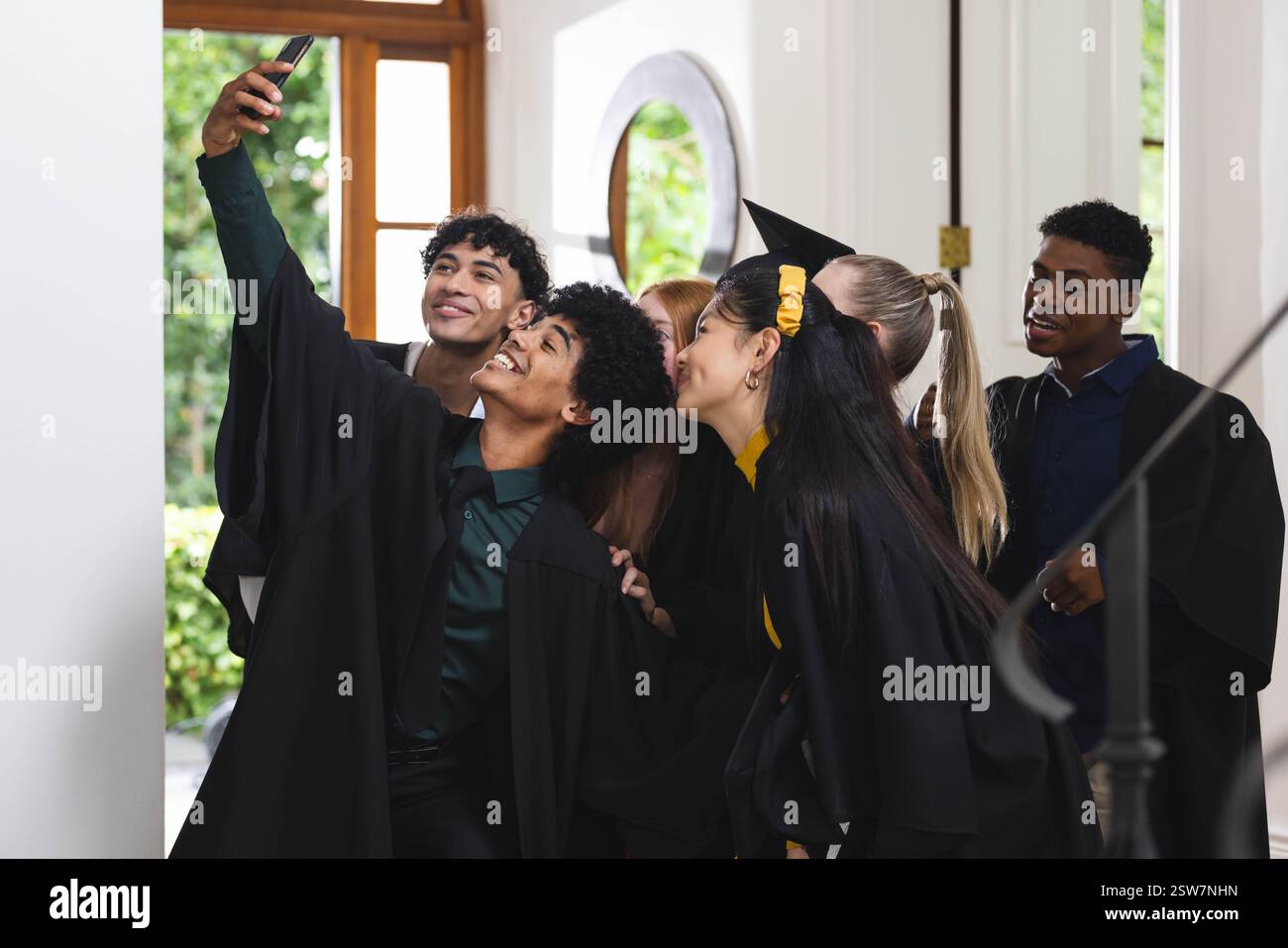Graduating diverse students taking selfie in caps and gowns ...