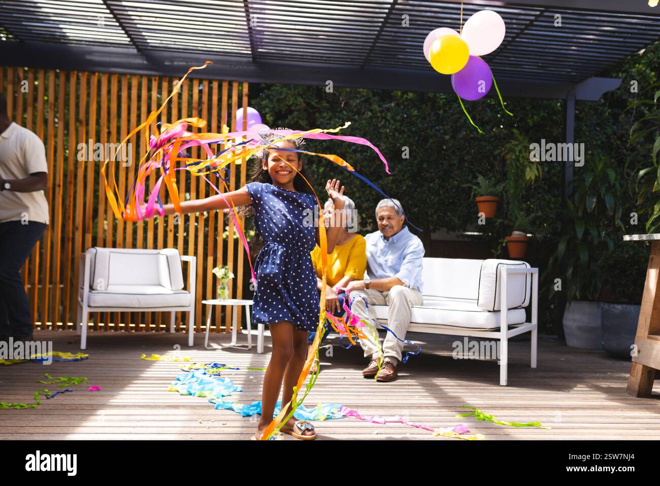 Young girl dancing with colorful streamers in garden, diverse family ...