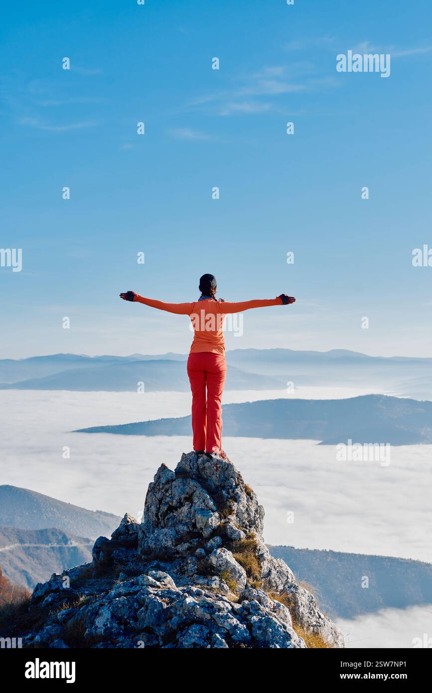 A fearless mountain climber stands on the edge of a rocky cliff, arms ...