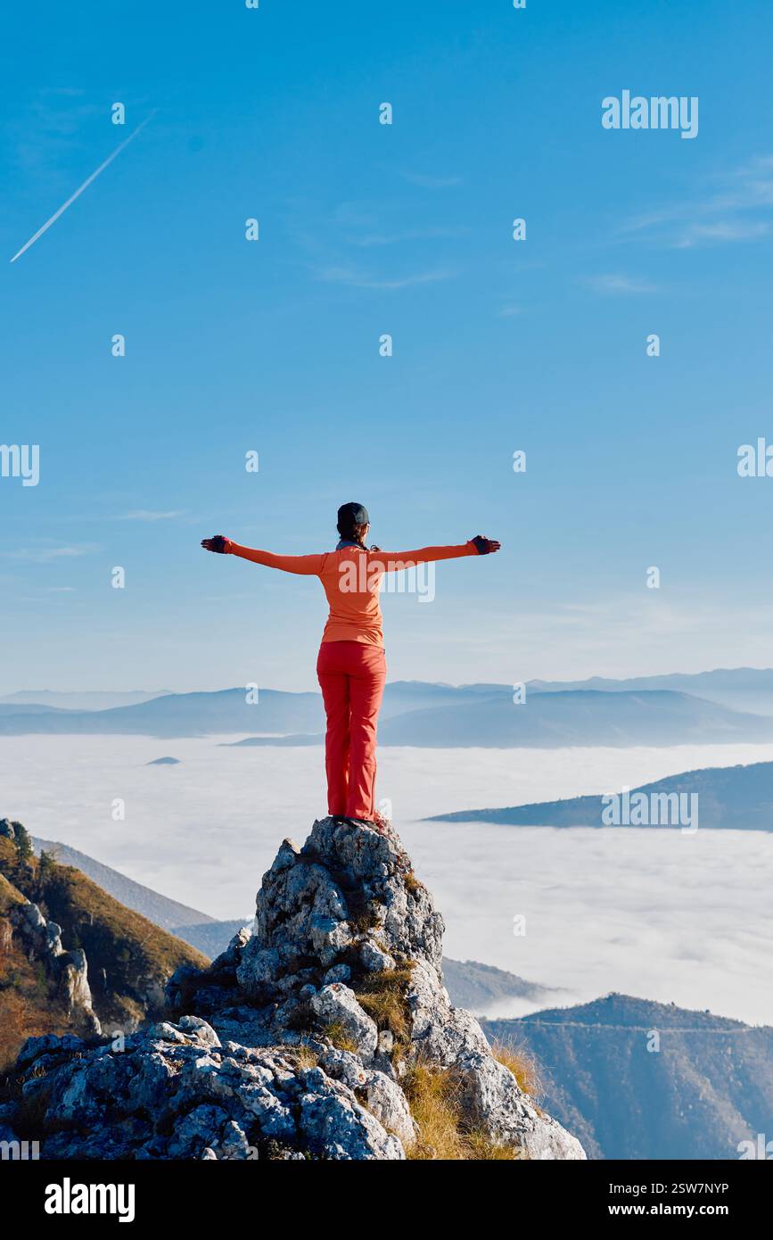 A fearless mountain climber stands on the edge of a rocky cliff, arms ...