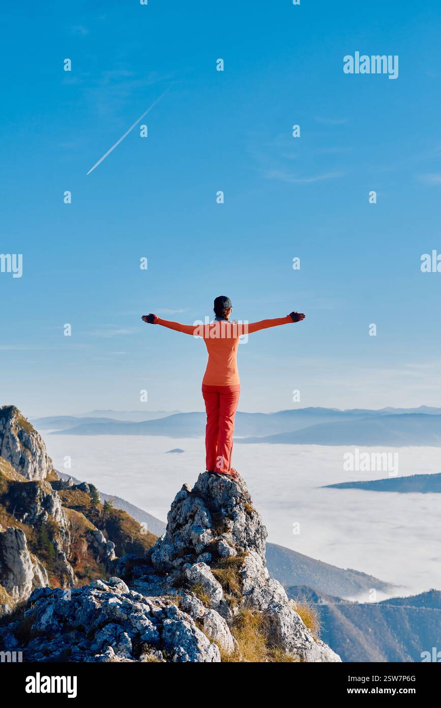 A fearless mountain climber stands on the edge of a rocky cliff, arms ...