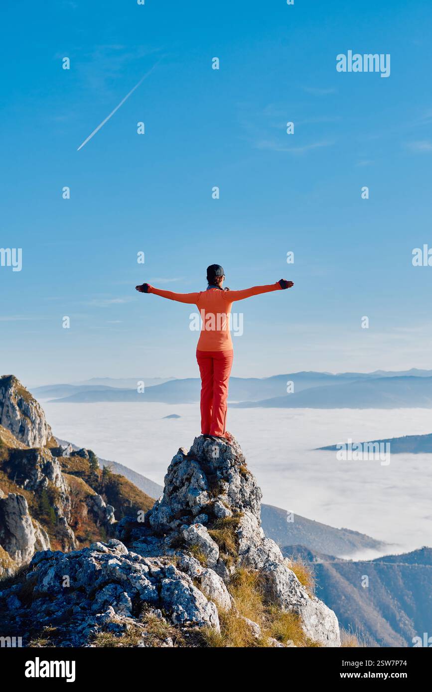 A fearless mountain climber stands on the edge of a rocky cliff, arms ...