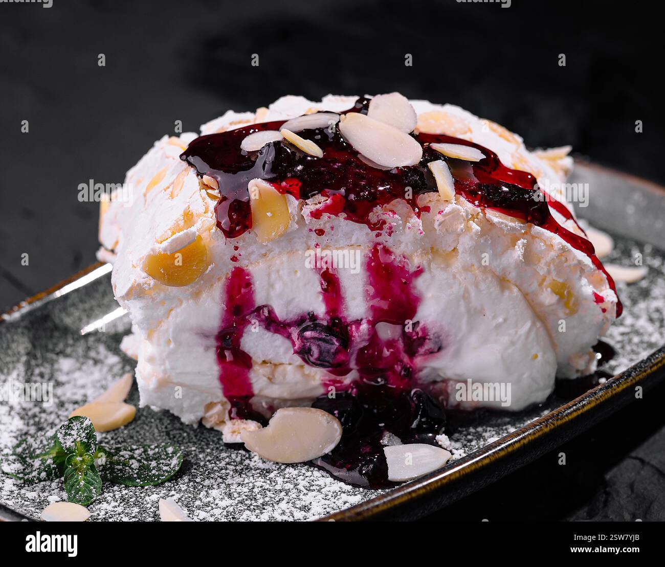 Elegant pavlova dessert topped with berry compote, sliced almonds, and ...