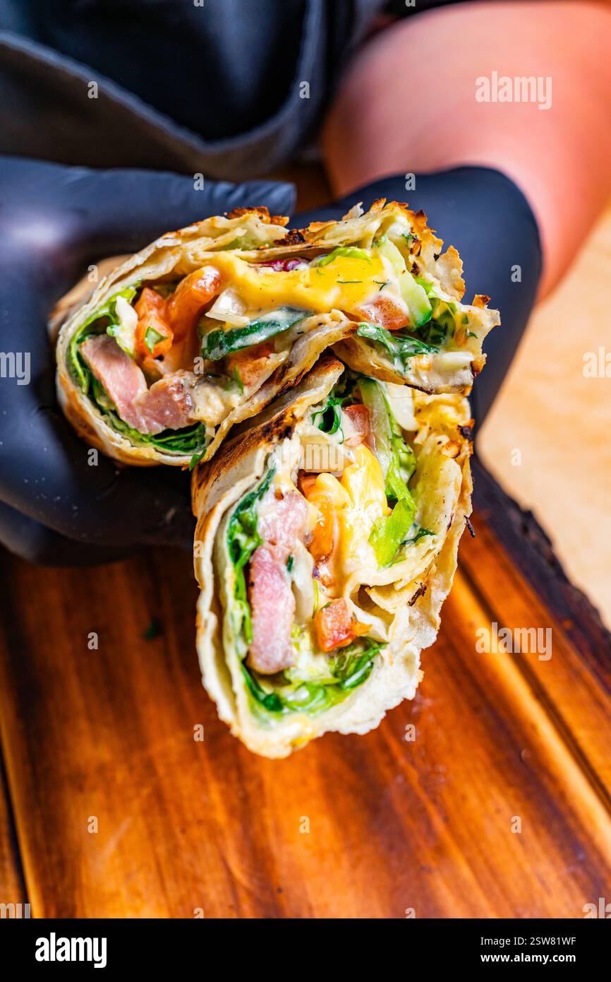 A person wearing black gloves holds a freshly made wrap filled with ...