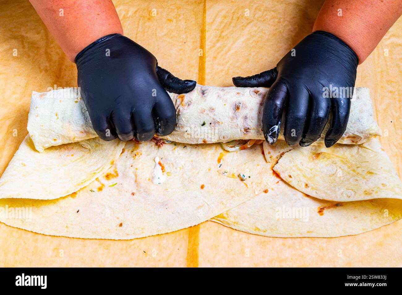 Hands wearing black gloves roll a freshly made wrap filled with savory ...