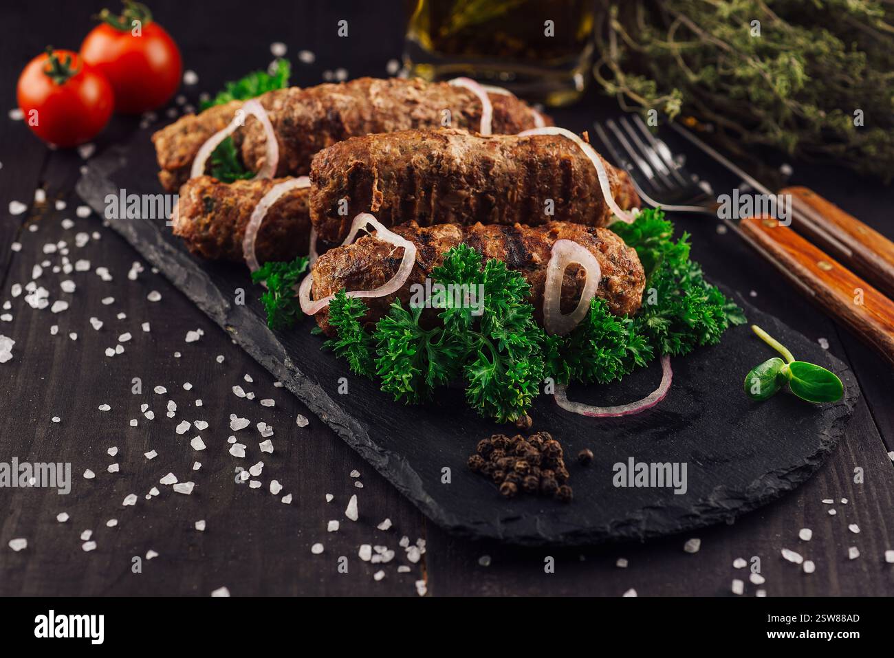 Grilled minced meat kebabs with red onions and herbs on a black slate ...