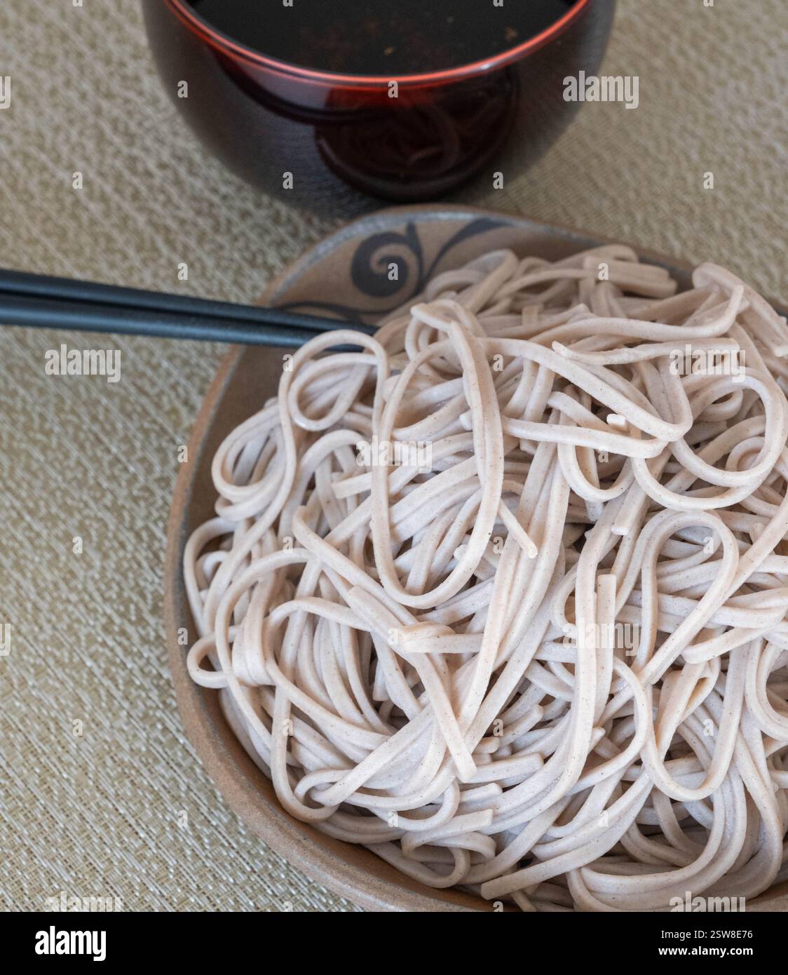 A plate with buckwheat soba noodles with chopsticks and sauce behind it ...