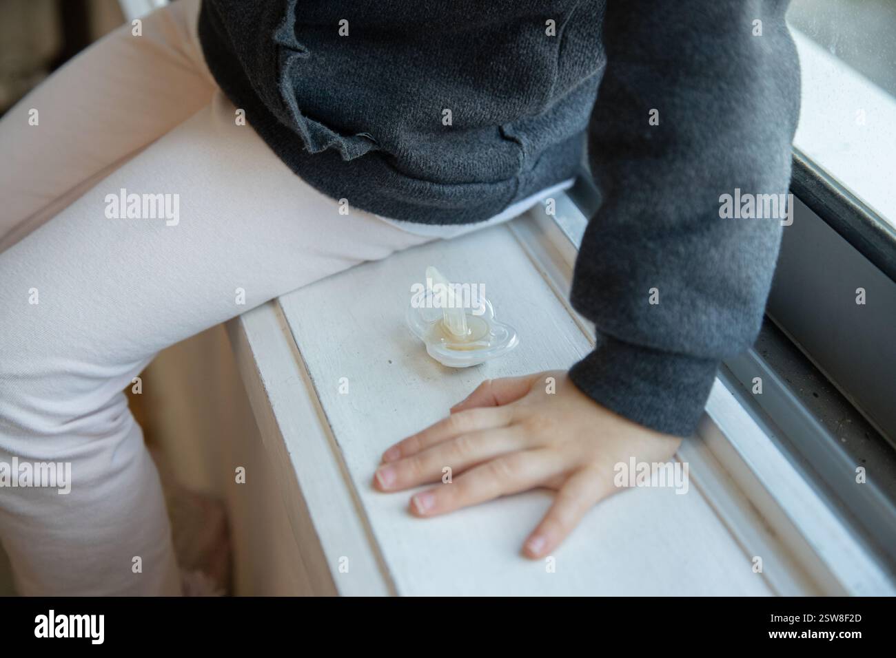 A child sits by the window, leaving a damaged pacifier behind Stock ...
