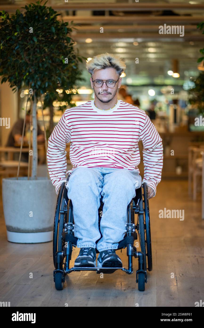 Confident disabled young man on wheelchair in cafe with adaptive ...