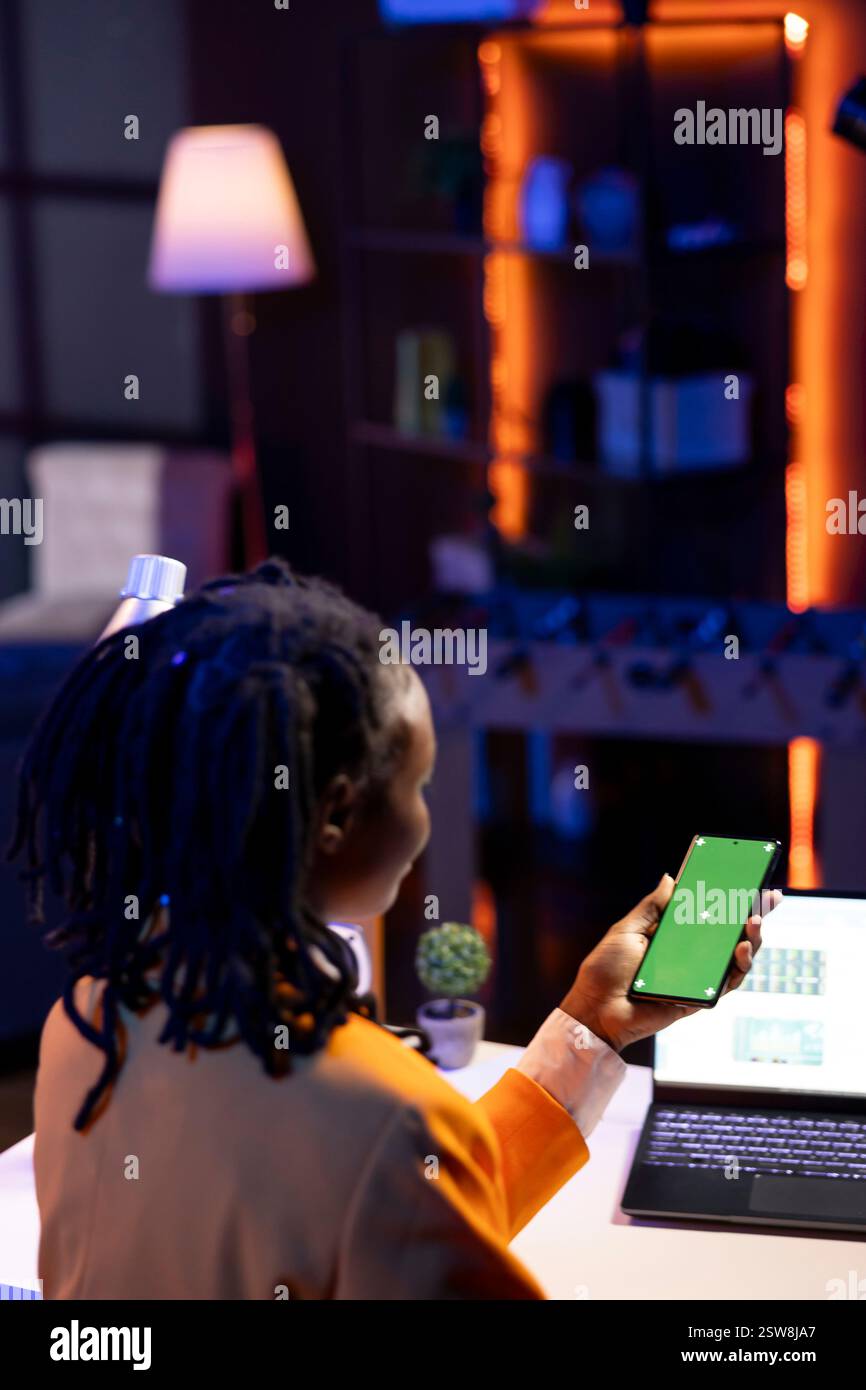 Green screen smartphone used by woman at laptop desk answering phone ...