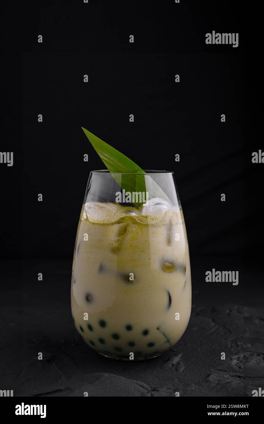 Glass of iced matcha latte with tapioca pearls is garnished with a palm ...