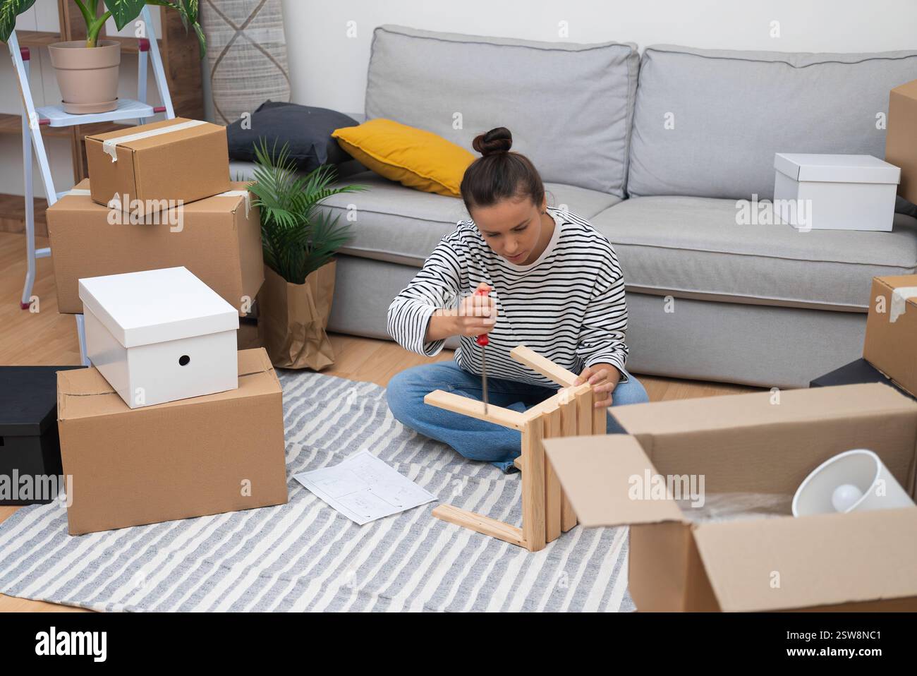 woman, amid moving carton boxes, sits on floor to assemble a self ...