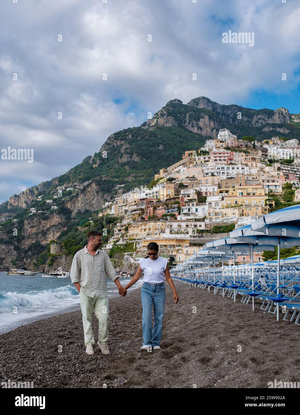 Couple strolling hand in hand along the pebble beach of Amalfi Coast ...