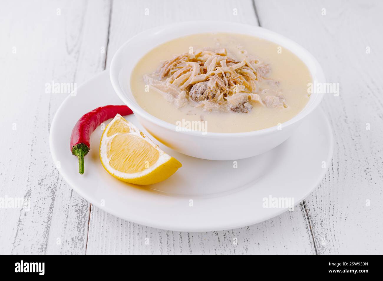 Turkish tripe soup is served on a white wooden table with lemon and ...