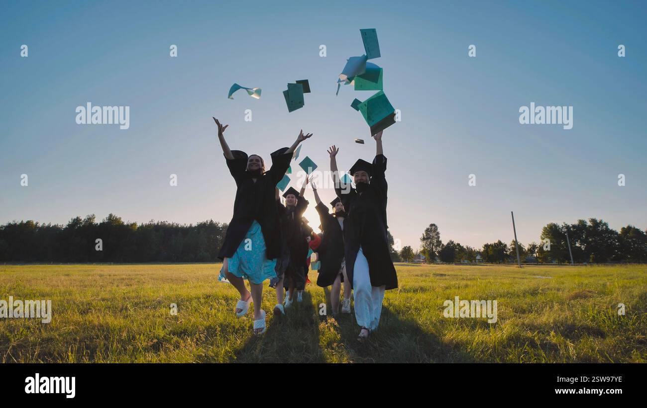 Happy students throwing their graduation caps into the air at sunset in ...