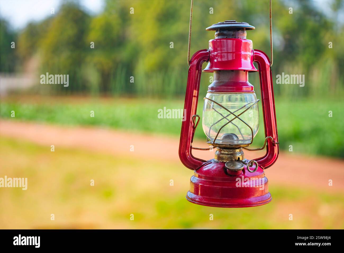 A vintage red kerosene lantern hangs outdoors against a blurred green ...