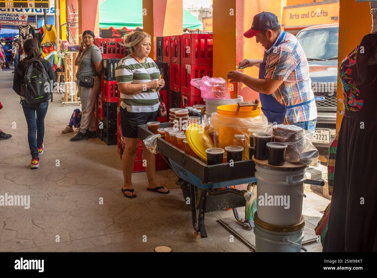 A vendor on a sidewalk fills a jar with honey to sell to a customer in ...