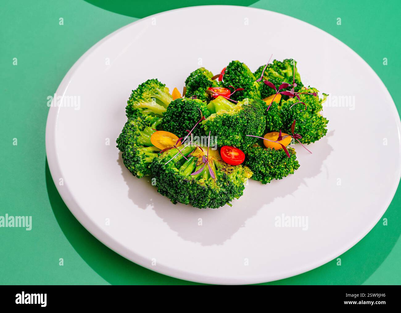 Steamed broccoli florets with tomatoes and microgreens on white plate ...
